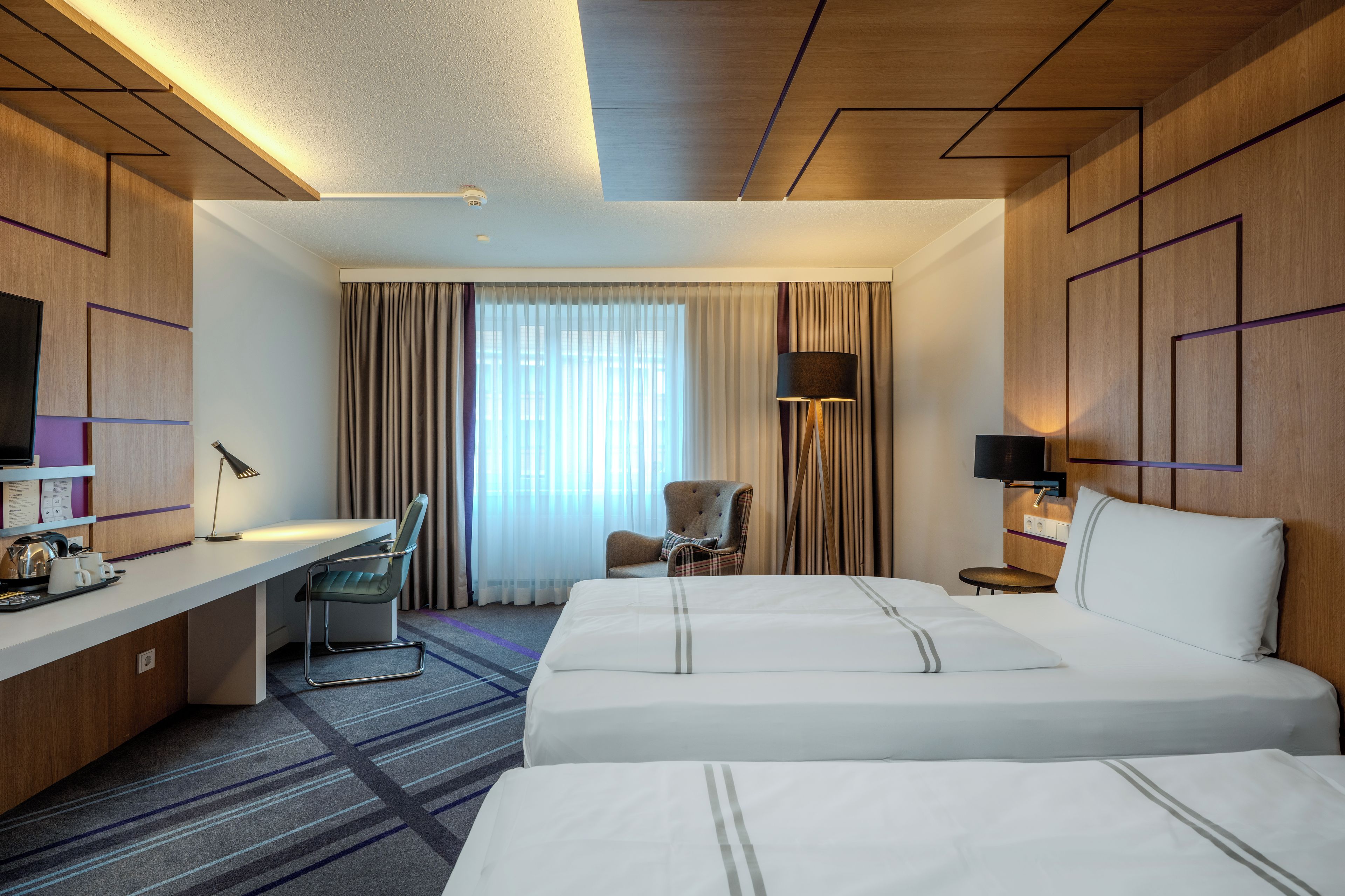 Quarto de hotel com duas camas, uma escrivaninha, uma cadeira, uma televisão e um abajur.
