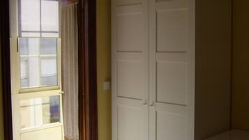 Quarto com guarda-roupa, pequeno armário e janela com cortinas.