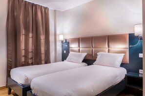 Quarto de hotel com duas camas de solteiro, cabeceira escura e mesa de cabeceira com abajur.