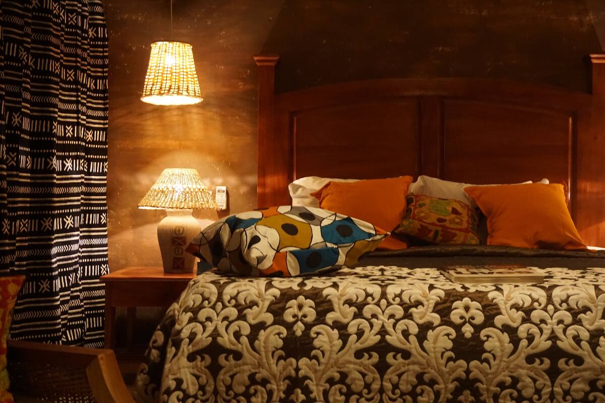 Quarto com colcha estampada, cabeceira de madeira e abajur.
