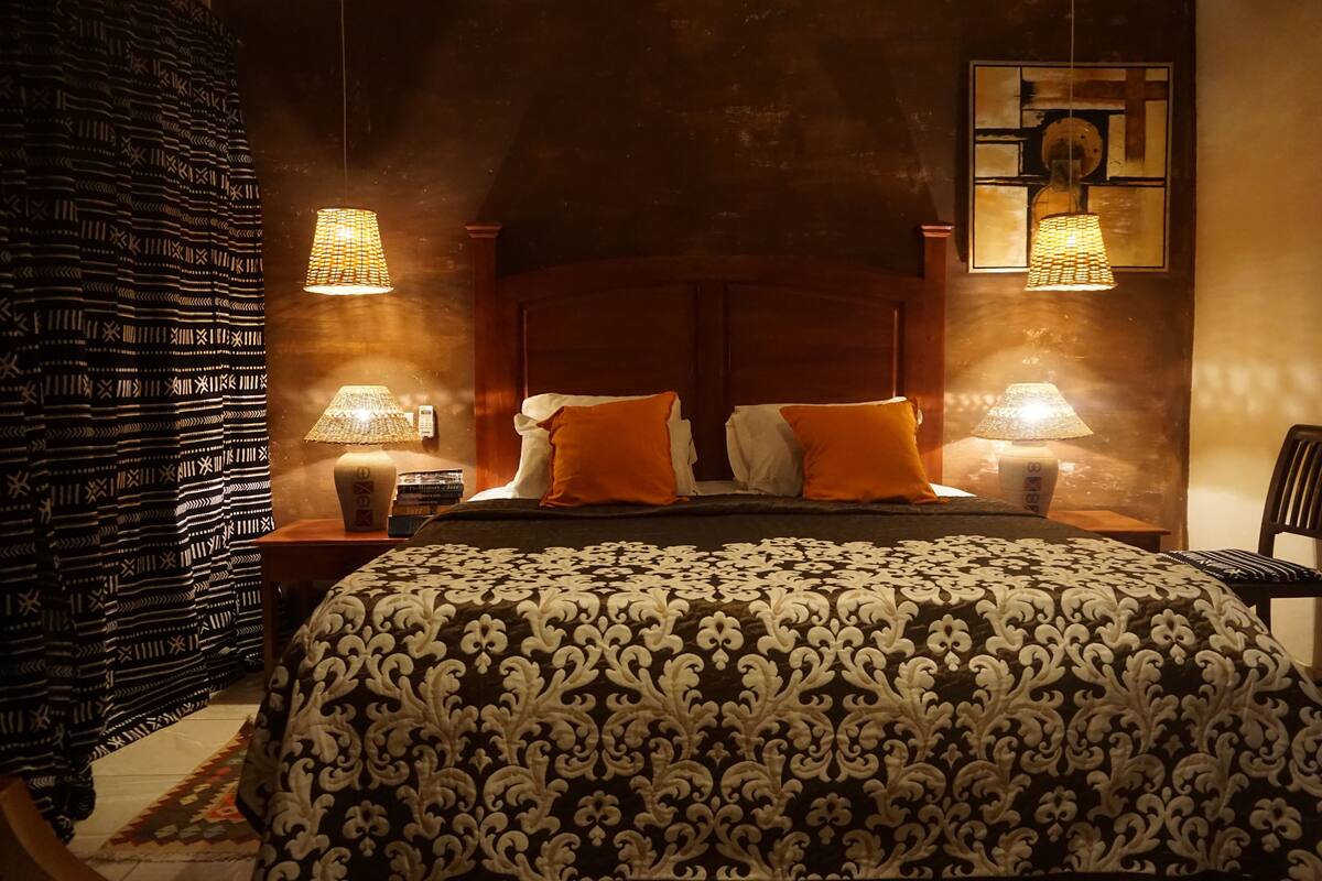Uma cama bem arrumada com um cobreleito estampado, duas almofadas e duas luminárias de cabeceira.