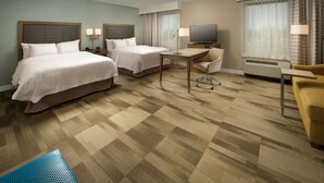 Quarto de hotel com duas camas, uma escrivaninha, uma televisão e uma cadeira.