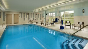 Uma piscina com água azul cristalina, rodeada por espreguiçadeiras e um guarda-sol.