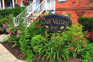 Placa do Oak Valley Inn cercada por vegetação exuberante e um edifício de tijolos.