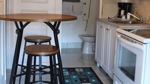 Uma cozinha compacta com uma mesa pequena e banquetas, micro-ondas, máquina de café e lava-louças.