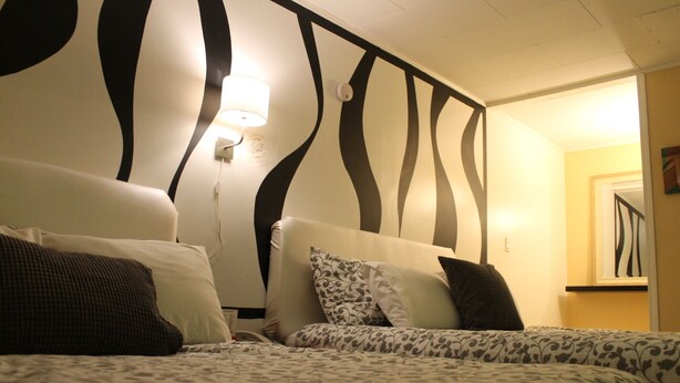 Quarto de hotel com duas camas, papel de parede listrado em zebra, luminária na parede e uma moldura com imagem.