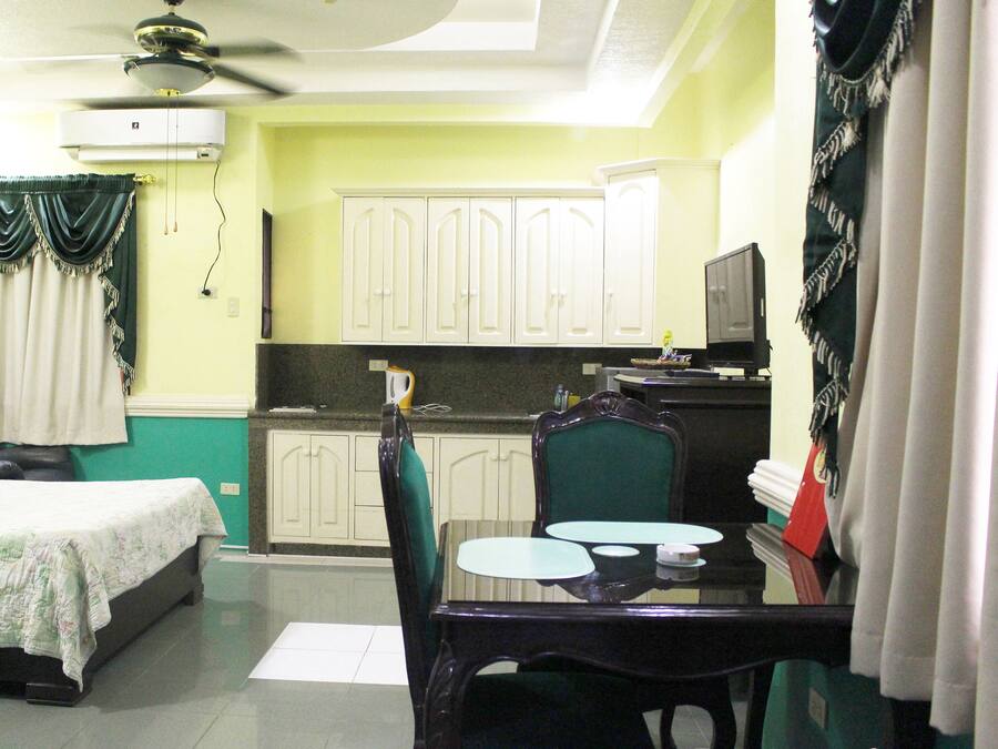 Quarto de hotel pequeno com uma cama, uma mesa de jantar com cadeiras, uma pequena cozinha e um ventilador de teto.