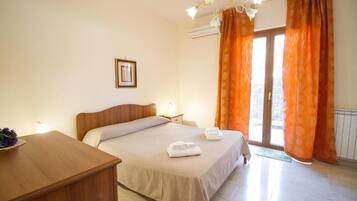 Um quarto com cama, mesas de cabeceira, um criado-mudo, cômoda de madeira e aparelho de ar condicionado.