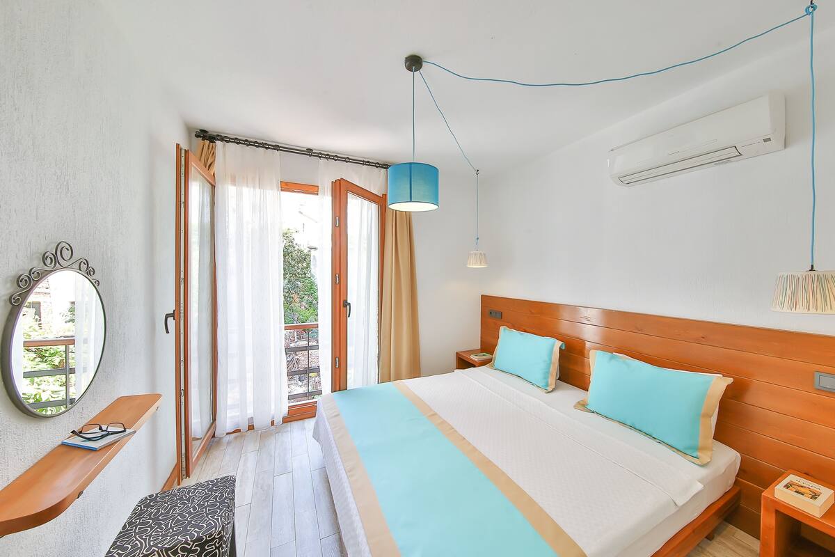Quarto de hotel com cama, mesas de cabeceira, espelho e vista para o exterior.