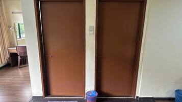 Entrada de hotel com duas portas marrons, um tapete na entrada e uma cesta de plástico no chão.