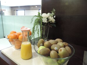 Uma bancada de cozinha com uma tigela de laranjas, um copo de suco de laranja, uma tigela de kiwis e um vaso com flores.