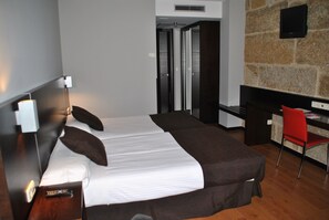 Quarto de hotel moderno com uma cama grande, uma mesa de escritório e um painel de parede em pedra.