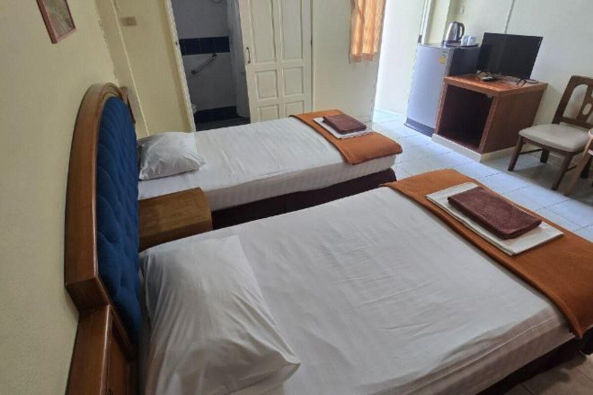 Quarto de hotel com duas camas de solteiro, uma escrivaninha com computador, uma cadeira e uma televisão.