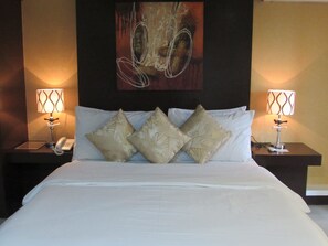 Quarto de hotel com cama grande, duas mesas de cabeceira com luminárias, um telefone e almofadas decorativas.