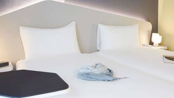 Quarto de hotel com cama, mesa de cabeceira e criado-mudo com luminária.