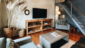 Uma sala de estar moderna com sofá, mesa de centro, televisão, estantes de madeira e uma escada.