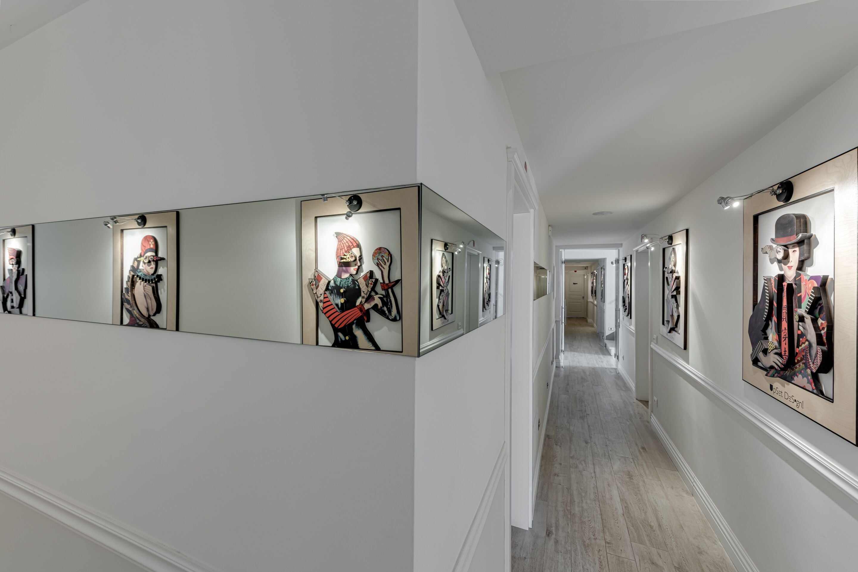 Corredor com obras de arte emolduradas nas paredes, que leva a um quarto.
