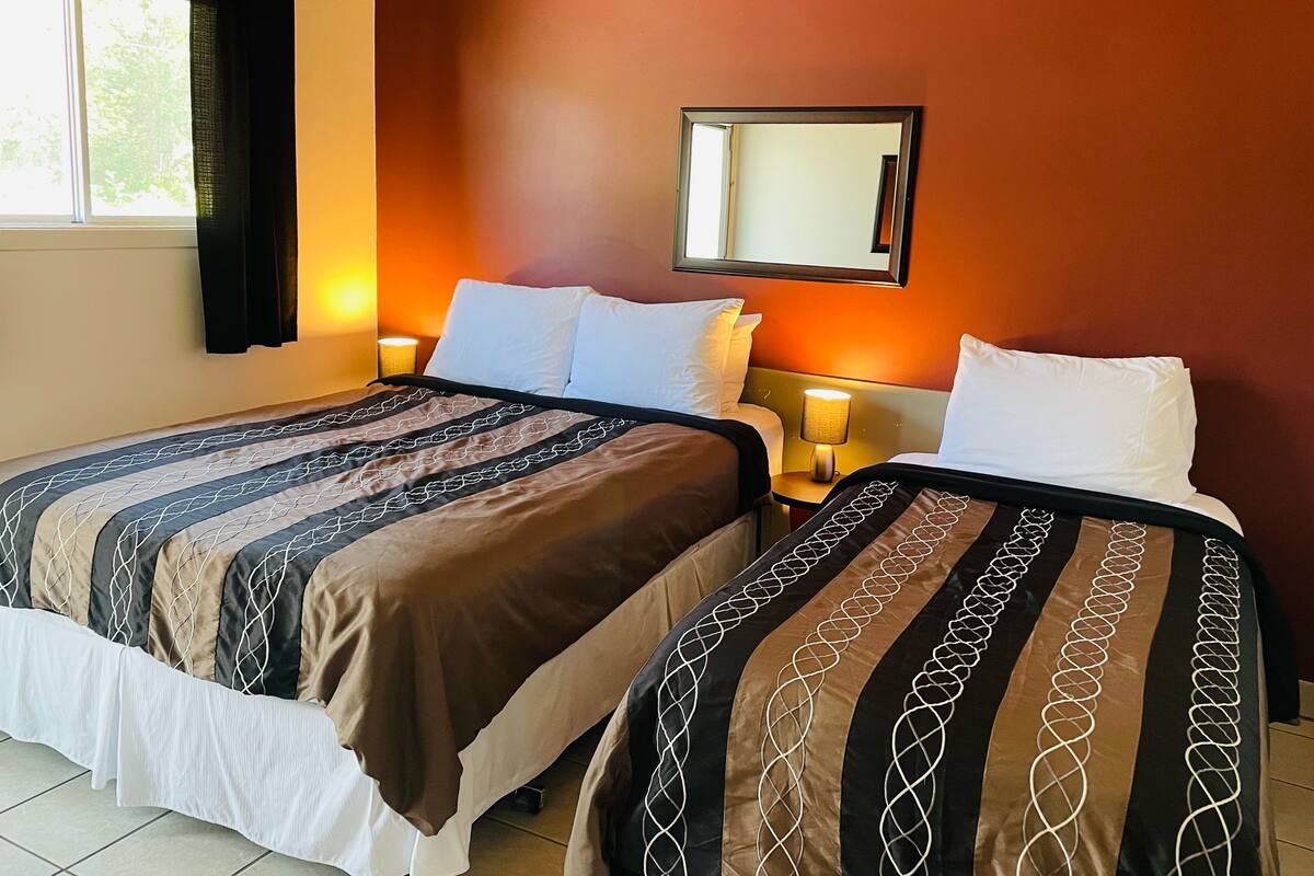 Quarto de hotel com duas camas, cada uma com roupa de cama estampada, luminária de cabeceira e espelho fixado na parede.