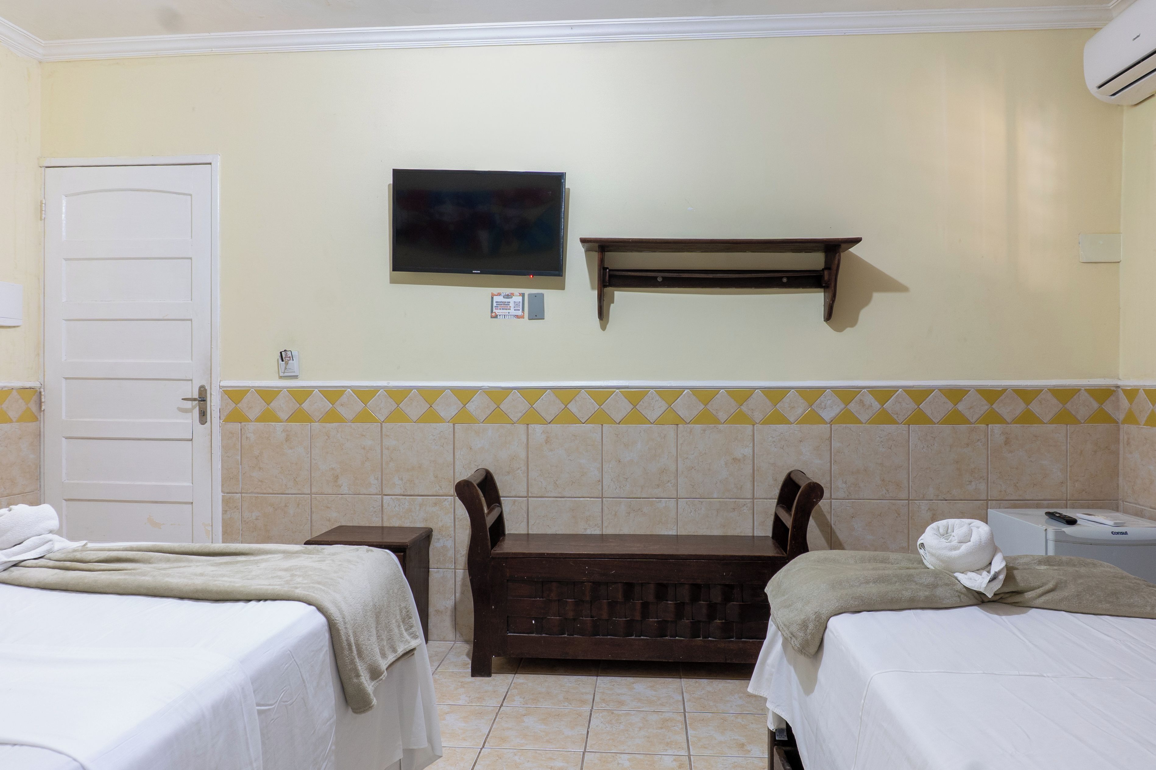 Quarto de hotel com duas camas, televisão, mesa pequena e máquina de lavar roupa.