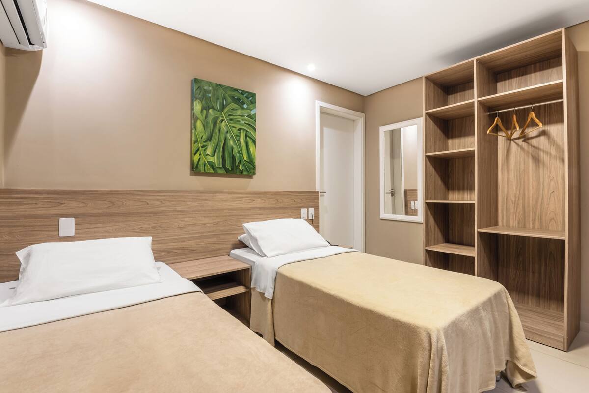 Quarto de hotel com duas camas, um guarda-roupa de madeira e um quadro na parede.