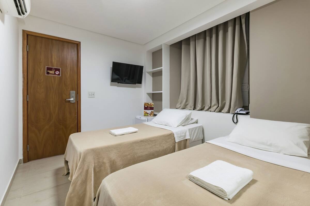 Quarto de hotel com duas camas, televisão, porta com placa e janela com cortinas.