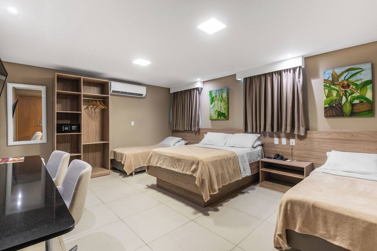 Quarto de hotel com duas camas, uma escrivaninha, um guarda-roupa e um quadro na parede.