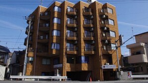 Um edifício de vários andares em tijolo, com varandas, entrada coberta e placas visíveis.