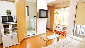 Sala de estar com sofá, mesa de centro de vidro, micro-ondas e televisão.
