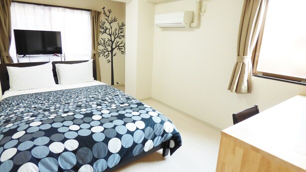 Quarto de hotel com cama, televisão, escrivaninha e janela com cortinas.