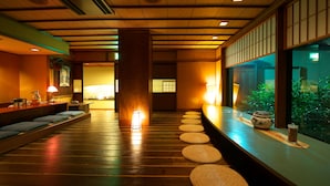 Quarto tradicional japonês com tatames, um balcão de recepção e vista para o verde lá fora.