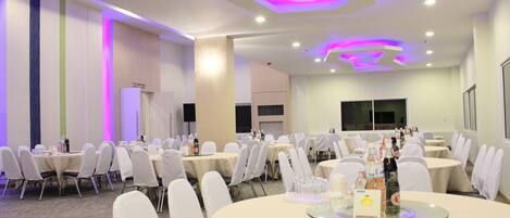 Uma sala de conferências com mesas redondas, cadeiras brancas e um palco.
