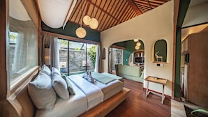 Quarto com cama grande, piso de madeira, área de refeições e vista para o exterior.