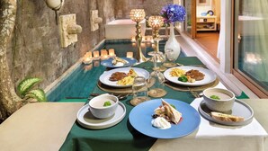 Mesa posta com pratos de comida, velas e objetos decorativos em um ambiente com parede de tijolos e uma janela grande.