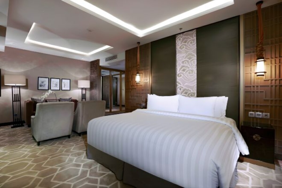 Quarto de hotel com uma cama grande, um sofá, uma mesa e uma luminária.