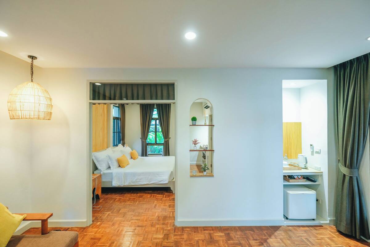 Quarto moderno com piso de madeira, cama com roupa de cama branca, mesa de cabeceira e luminária pendente.
