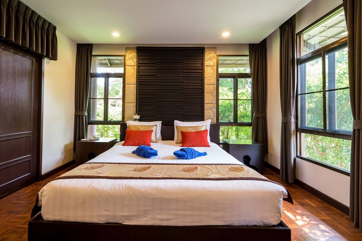 Quarto de hotel com uma cama grande, duas mesas de cabeceira, uma janela com cortinas e vista para o verde lá fora.