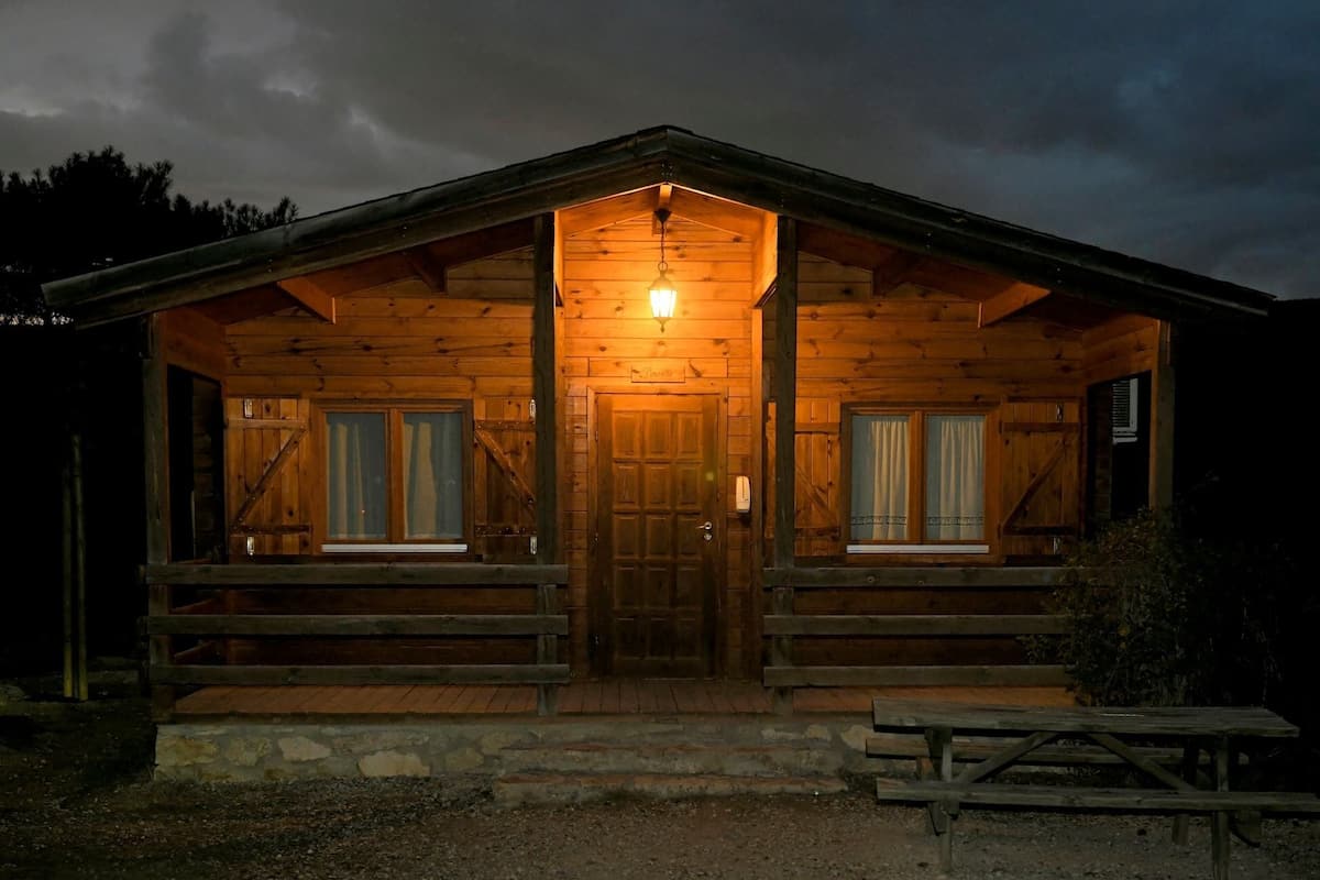 Uma cabana de madeira com varanda, porta da frente e um banco na parte externa.