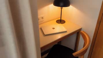 Um laptop sobre uma mesa com uma lâmpada, uma cadeira e uma tomada.