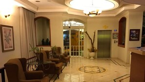 Um saguão de hotel com balcão de recepção, área de estar e um lustre grande.