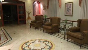 Um hall espaçoso com piso de azulejos, um padrão circular decorativo e três poltronas marrons dispostas ao redor de uma mesinha.