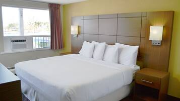 Quarto de hotel com uma cama grande, uma mesa de cabeceira, cortinas em uma janela e luminária na parede.