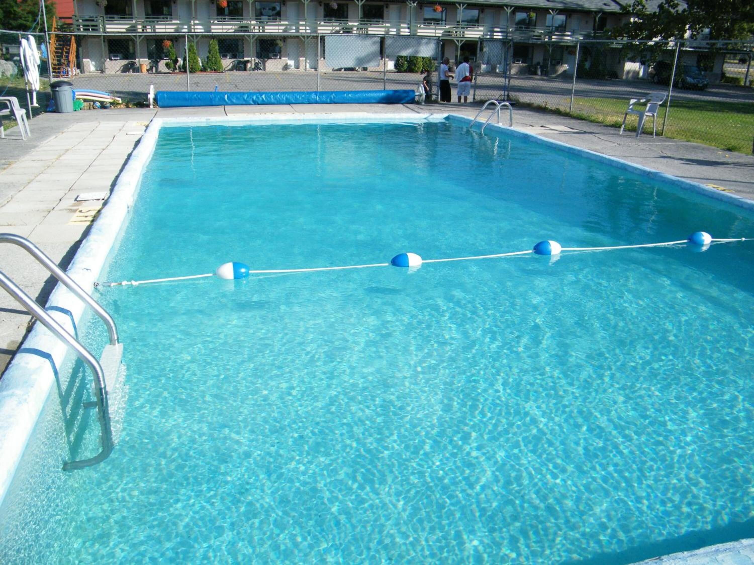 Piscina azul cristalina com escada e barreiras flutuantes.