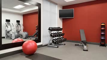 Uma academia com equipamentos de ginástica, uma televisão na parede e um espelho.