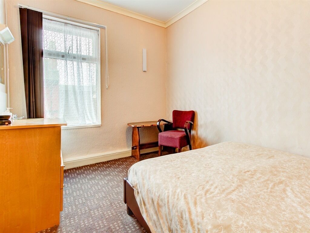 Quarto de hotel com cama, escrivaninha, cadeira e janela com cortinas.