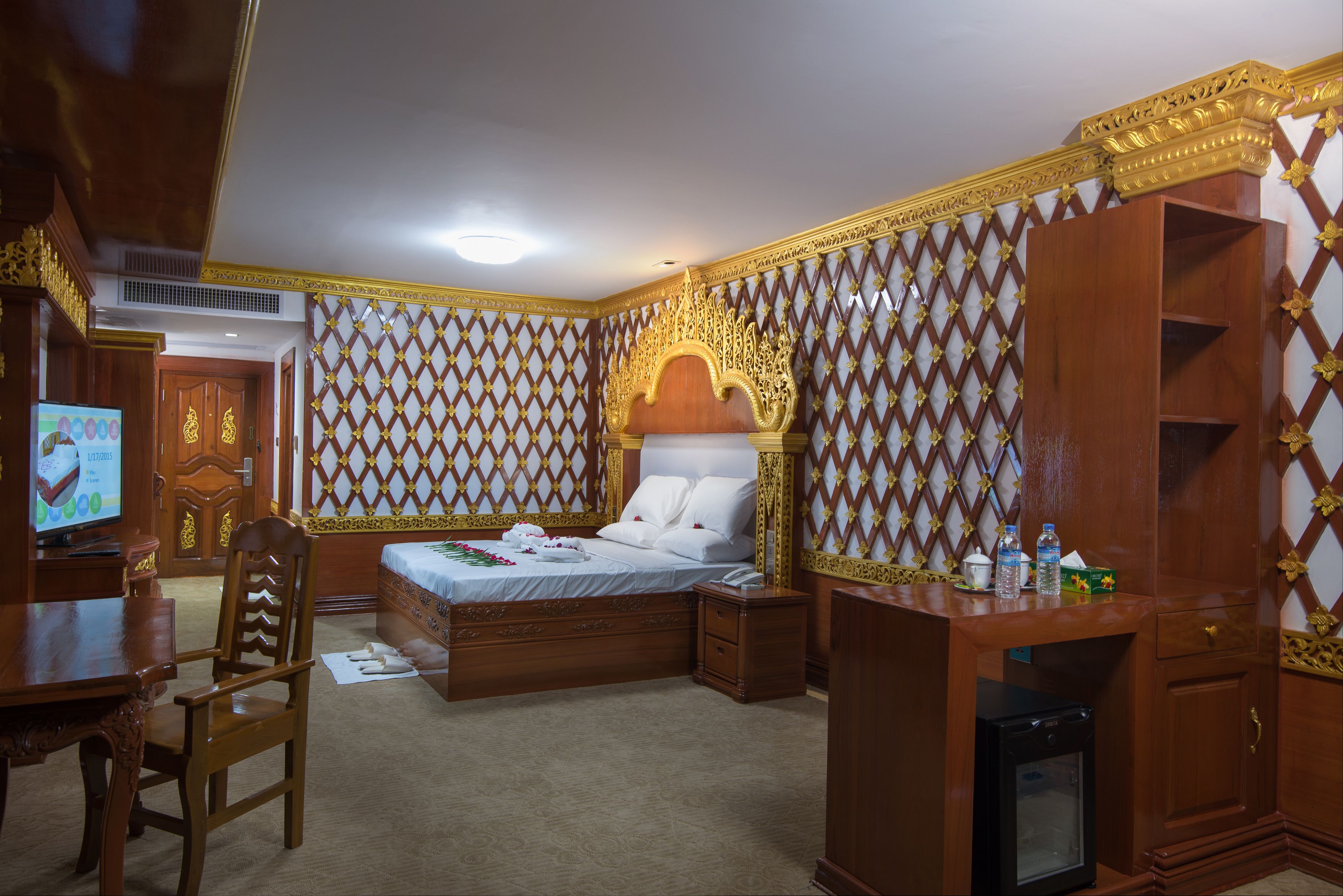 Quarto de hotel com cama de madeira, uma secretária com televisão e um minibar.
