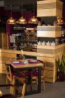 Uma área de bar com balcão de madeira, prateleiras empilhadas, luminárias pendentes e uma mesa posta para refeições.