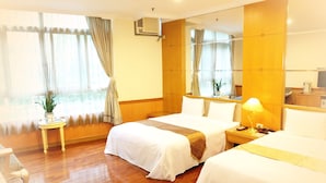 Quarto de hotel com duas camas, uma mesa de cabeceira com abajur, uma mesinha com uma planta e um espelho grande.