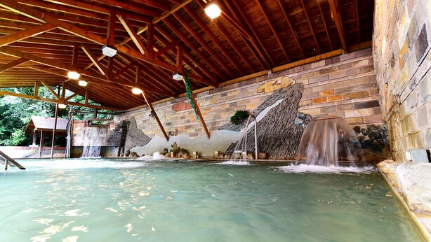 Piscina coberta com várias cascatas, vigas de madeira e paredes de pedra.