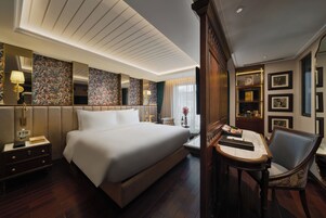 Quarto de hotel com uma cama grande, uma escrivaninha com cadeira, mesa de cabeceira, espelho e parede com quadros.