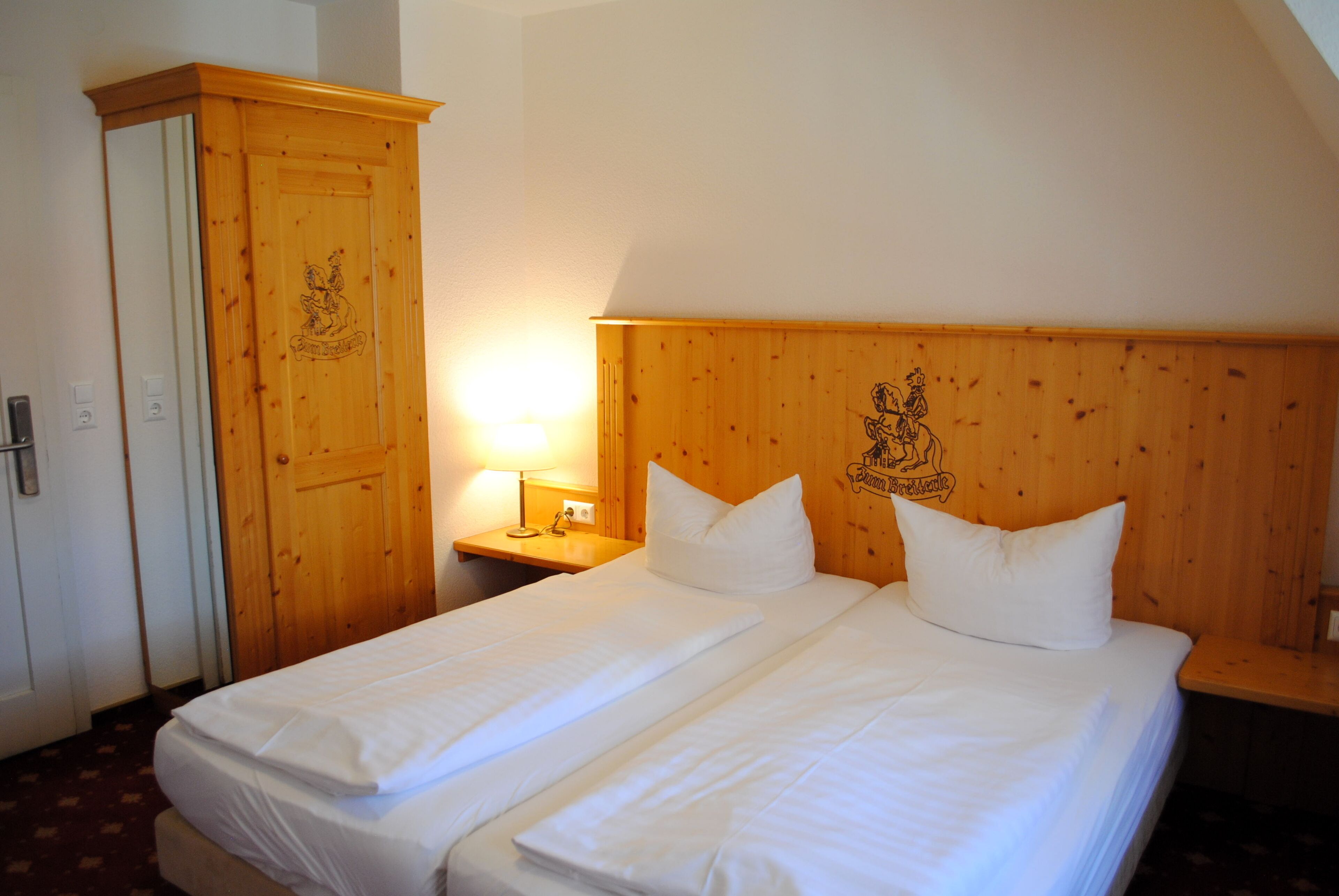 Uma cama de casal com lençóis brancos em um quarto com lambris e um guarda-roupa de madeira.